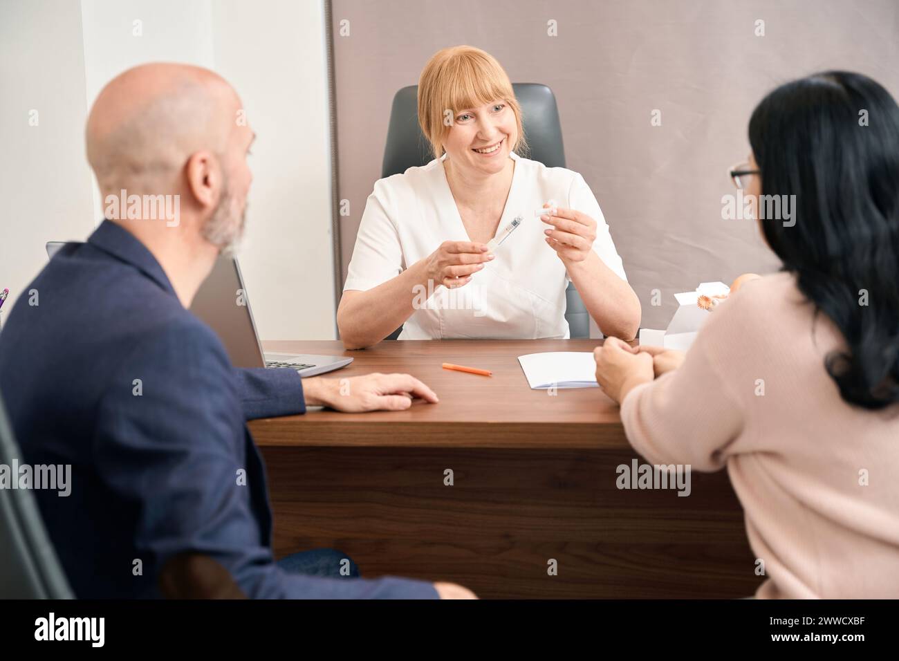 Woman reproductologist showing to female client special syringe with ...