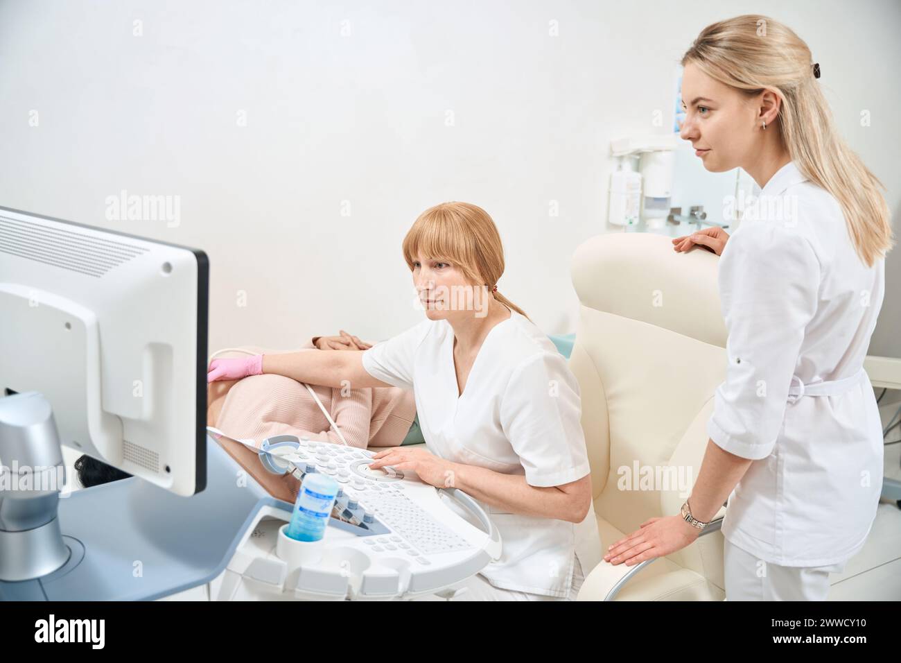 Female assistant and doctor sonographer examining thyroid gland of ...