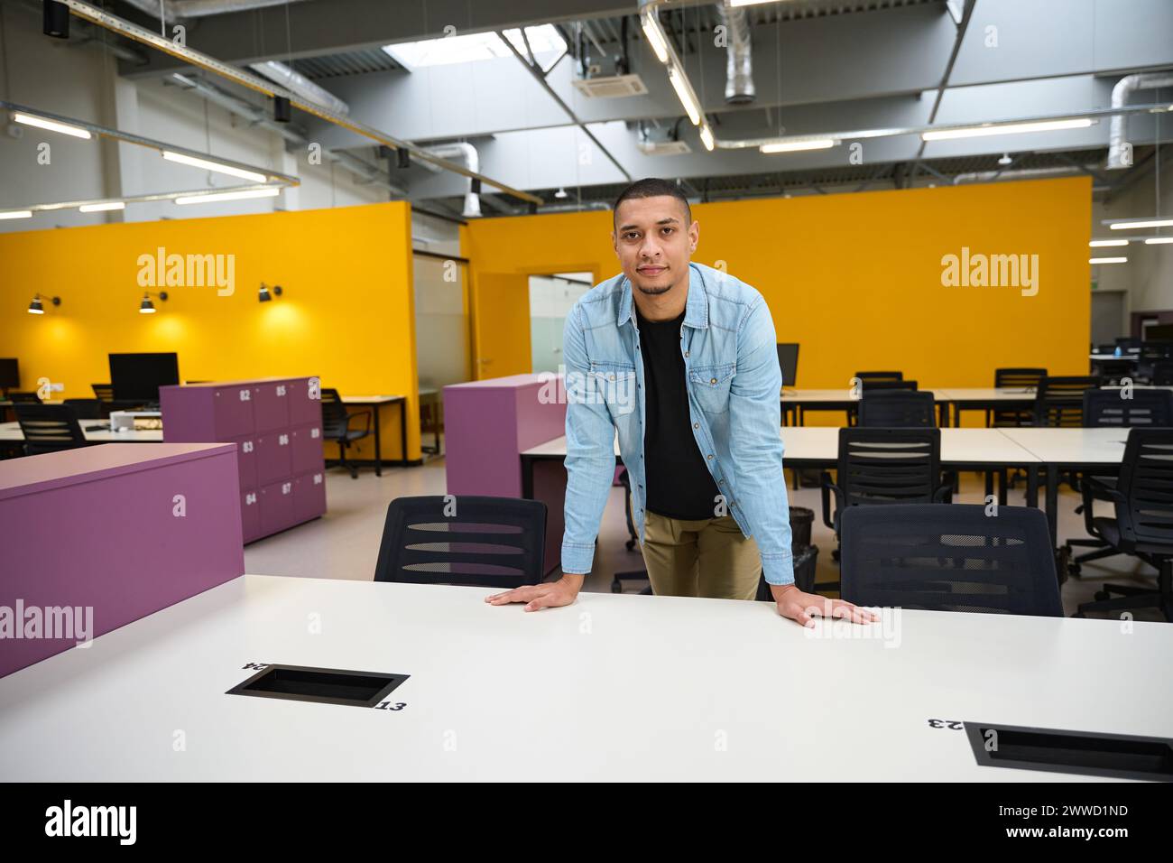 Joyful young man leaning on table while standing at office Stock Photo ...