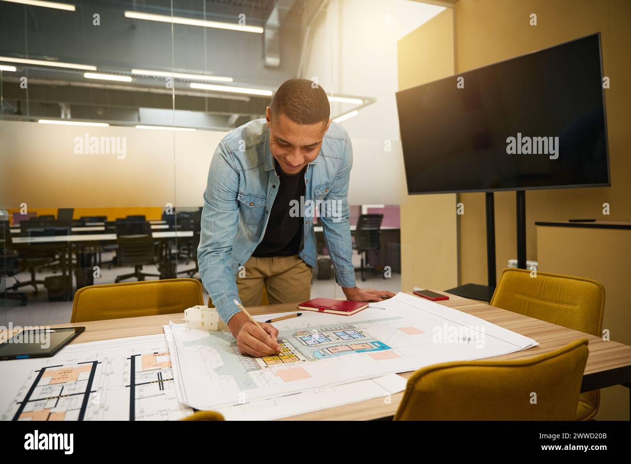 Happy young architect bending over table and working with plan Stock ...