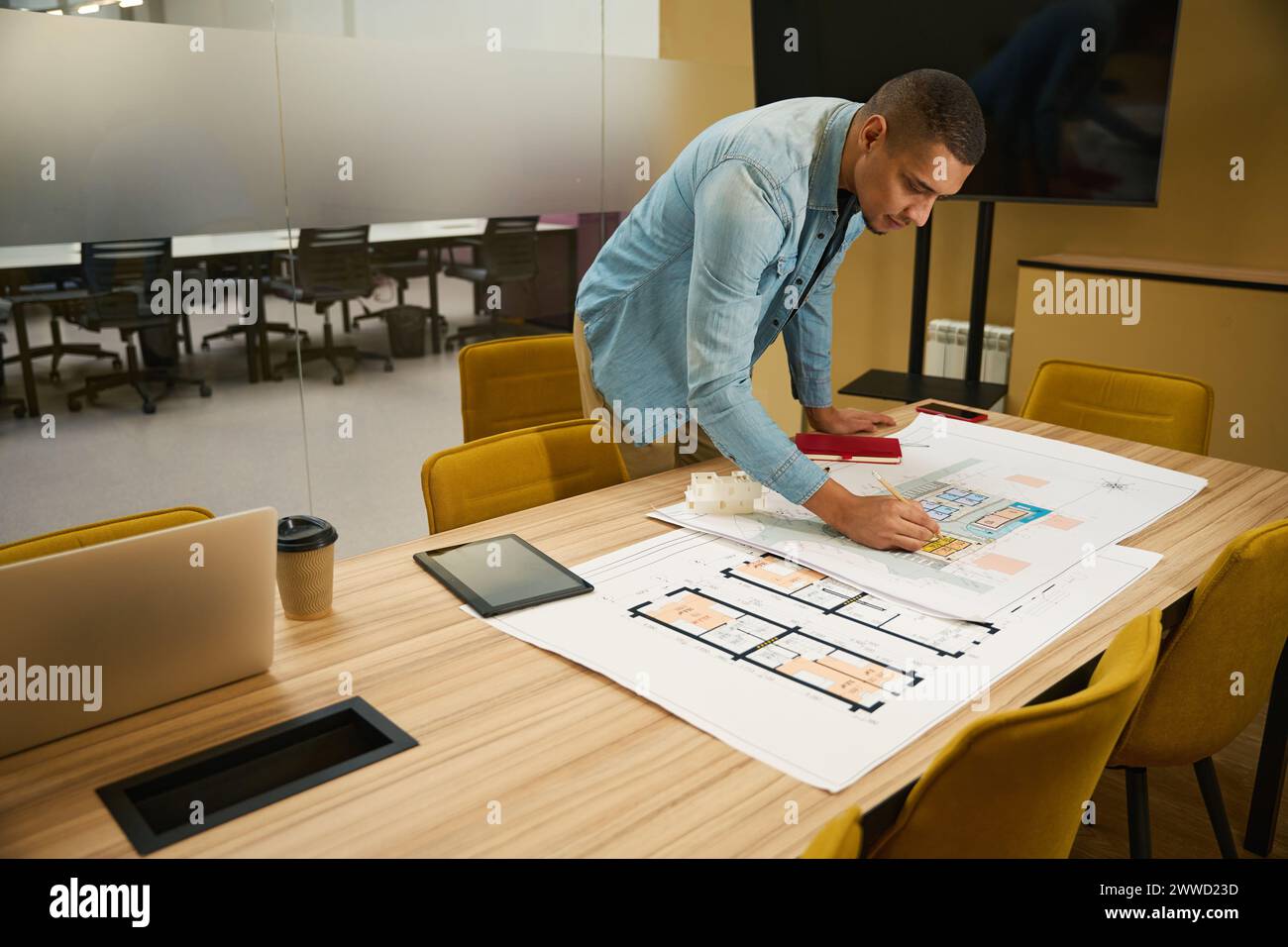 Concentrated young man standing behind desk and correcting building ...