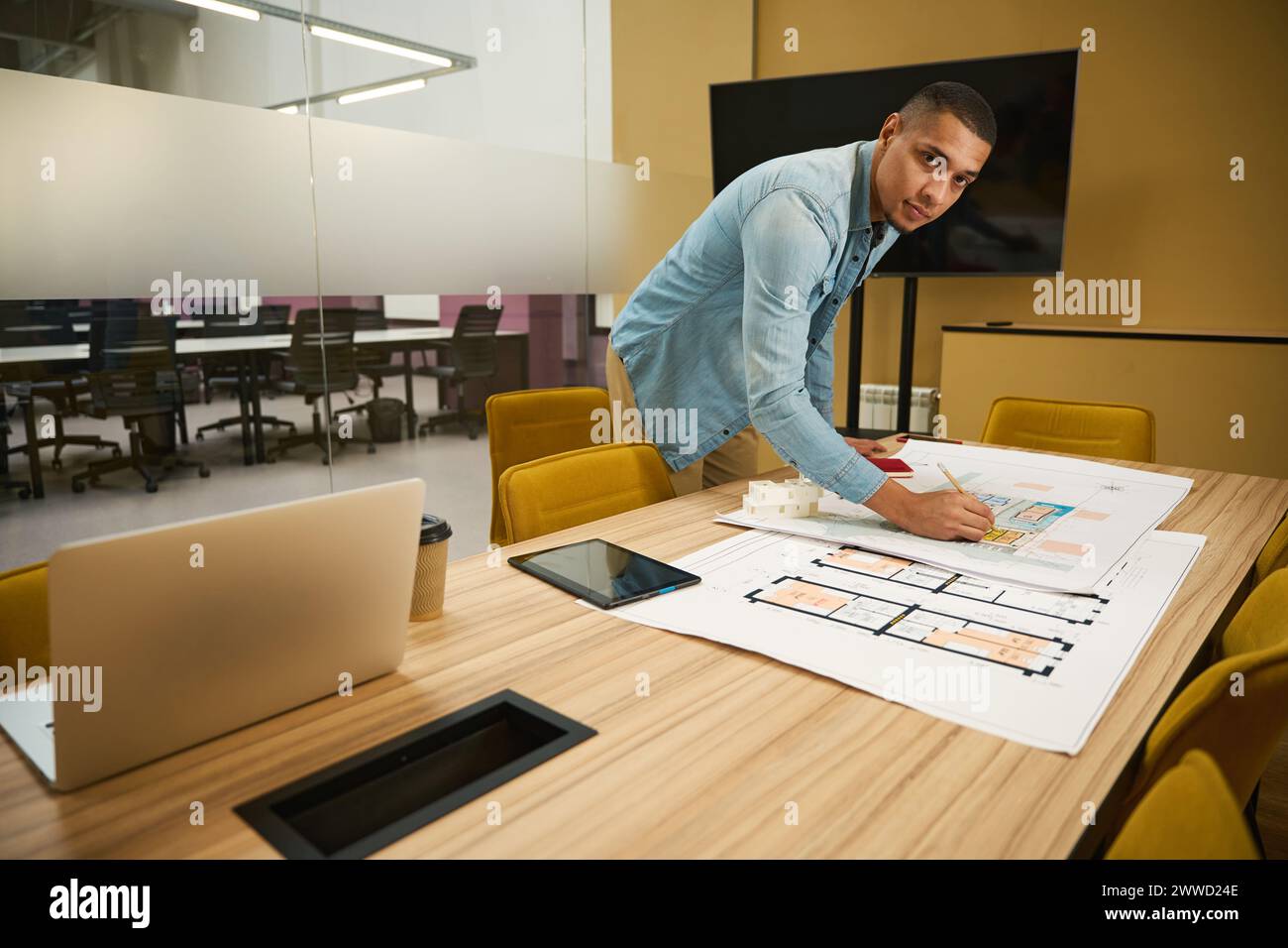 Serious guy bending over table while writing something on blueprint ...