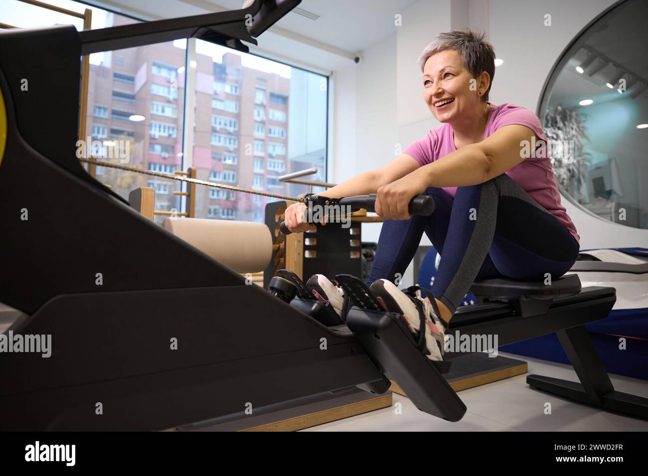 Adult smiling caucasian woman doing sport exercise for back on rowing ...