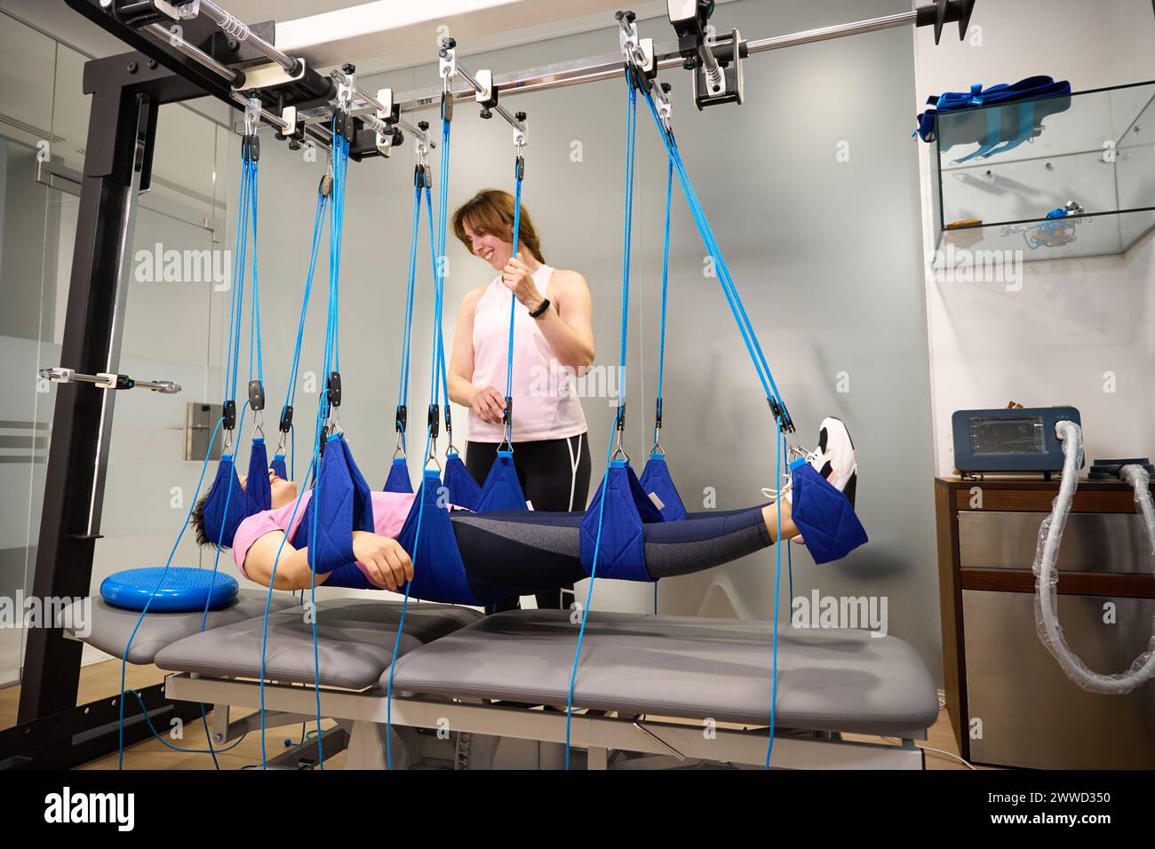 Smiling female trainer helping adult woman hanging on suspension ...