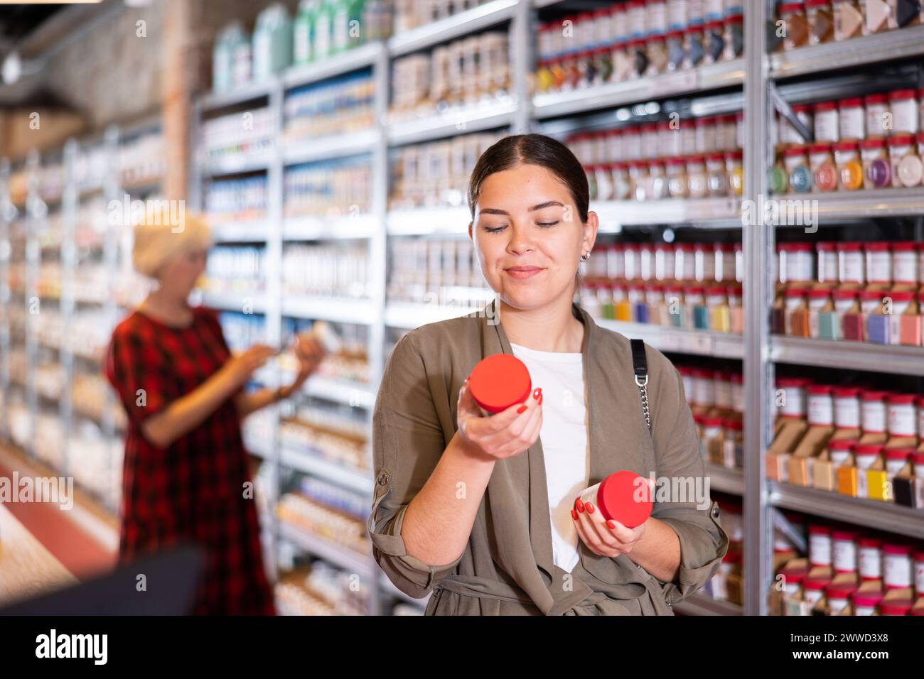 Female shopper choosing pottery glaze jars in pottery specialty store ...