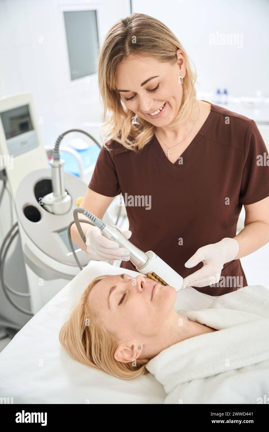 Smiling phlebologist using endosphere therapy on the young adult woman ...