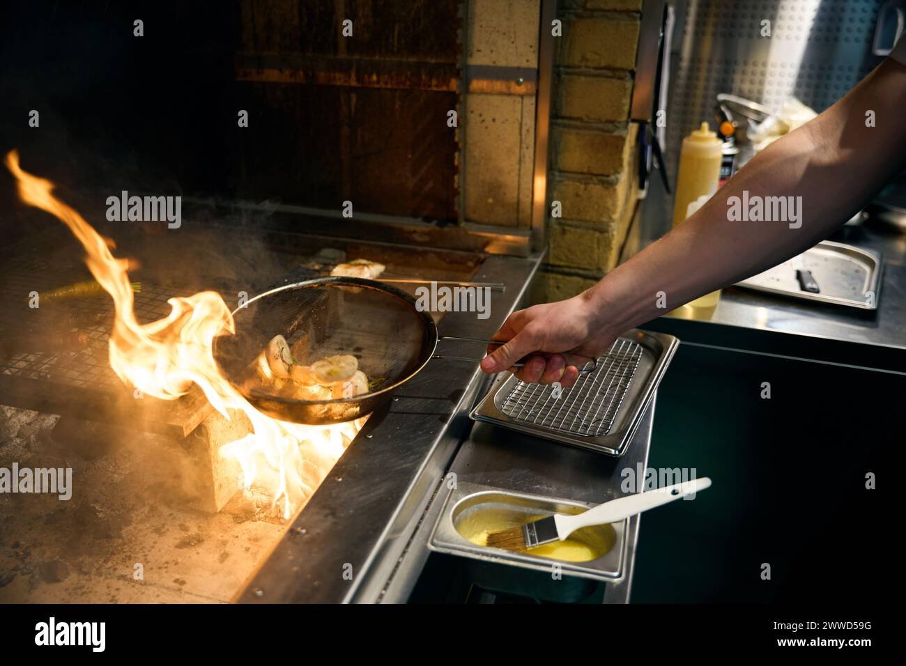 Side view of partial male chef frying onions and carrots in burning ...