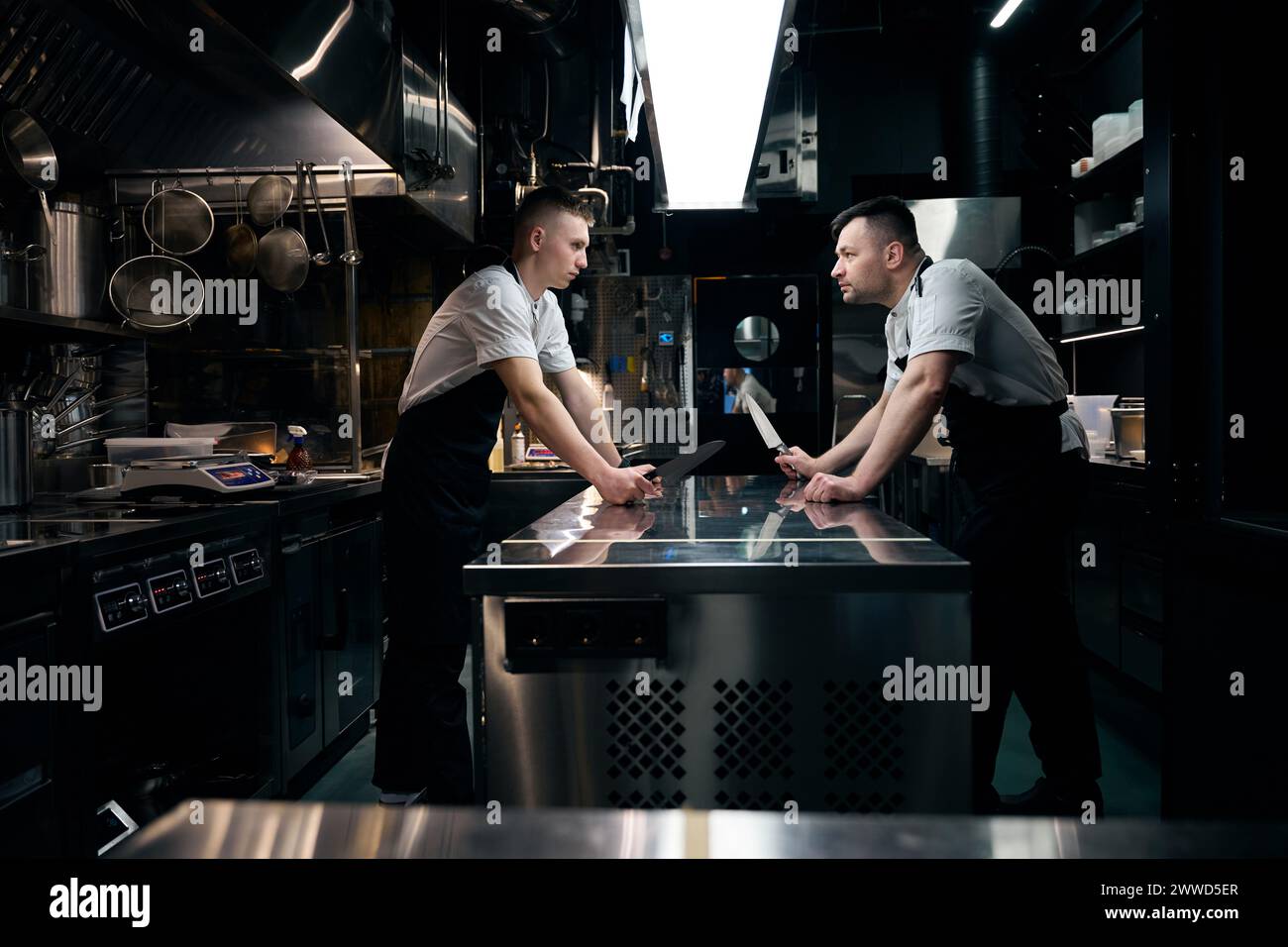 Two serious male competitor chefs with knives looking at each other at ...