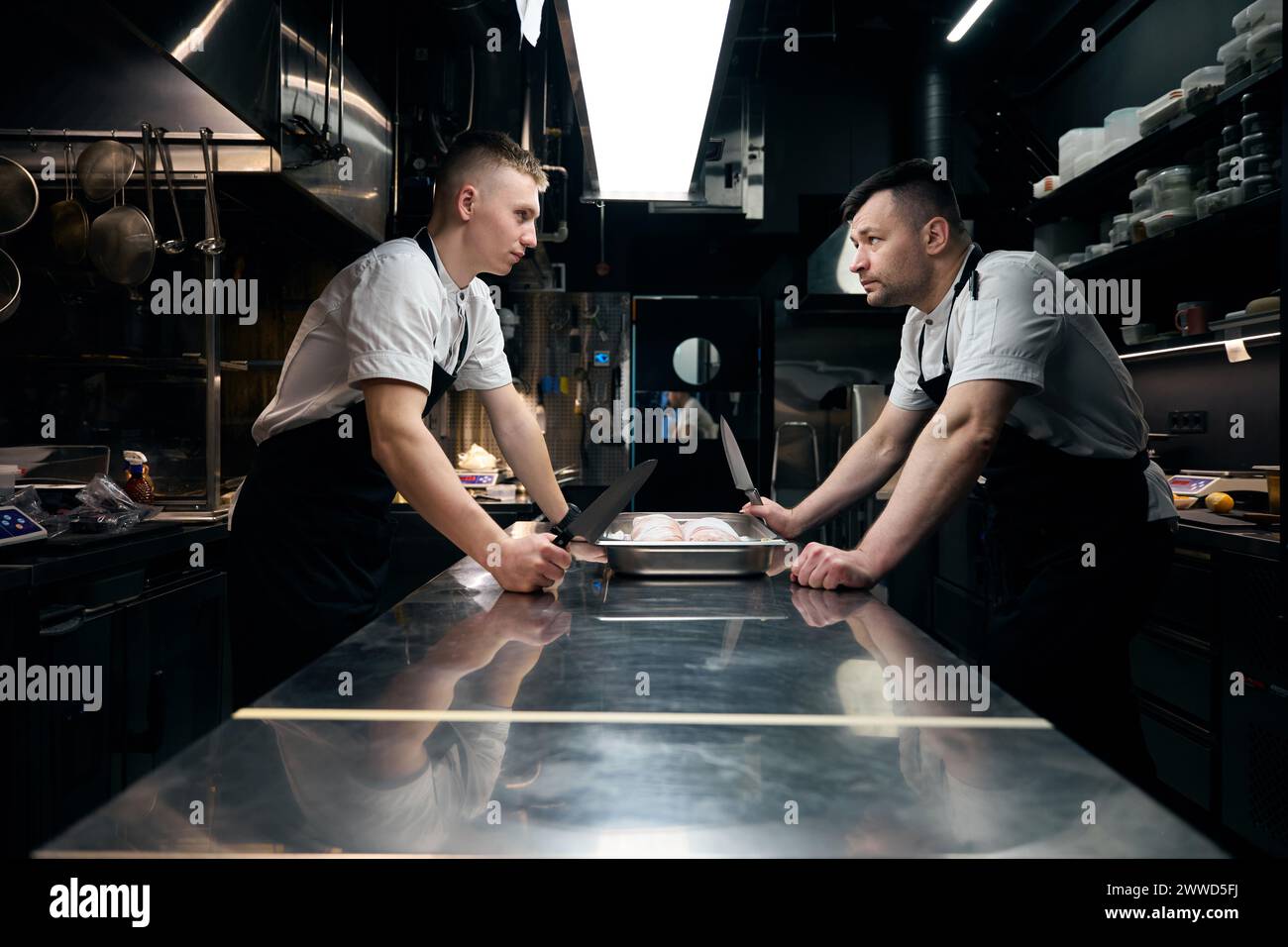 Two male competitor chefs with knives looking at each other in ...
