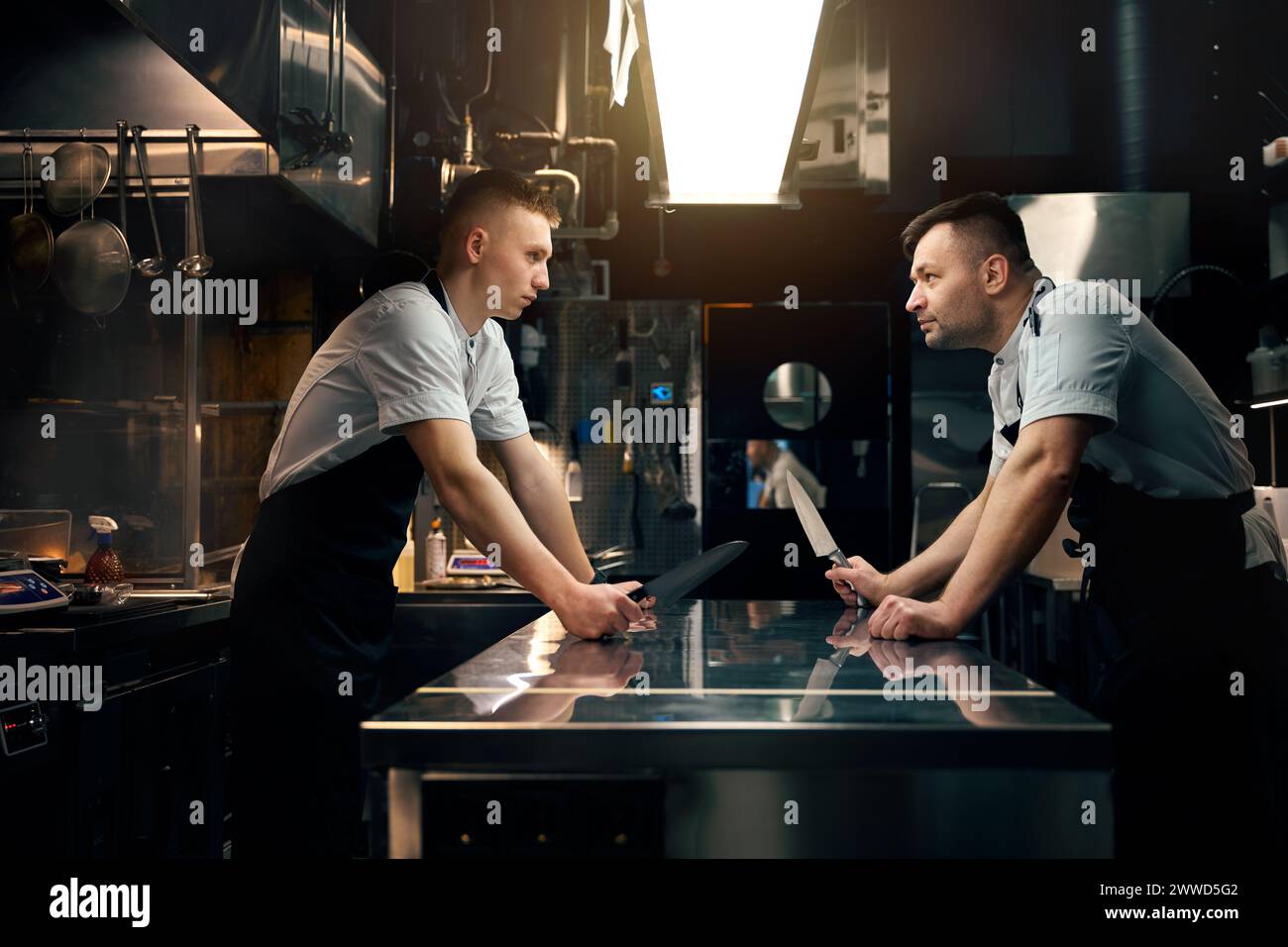 Side view of two serious male competitor chefs with knives looking at ...