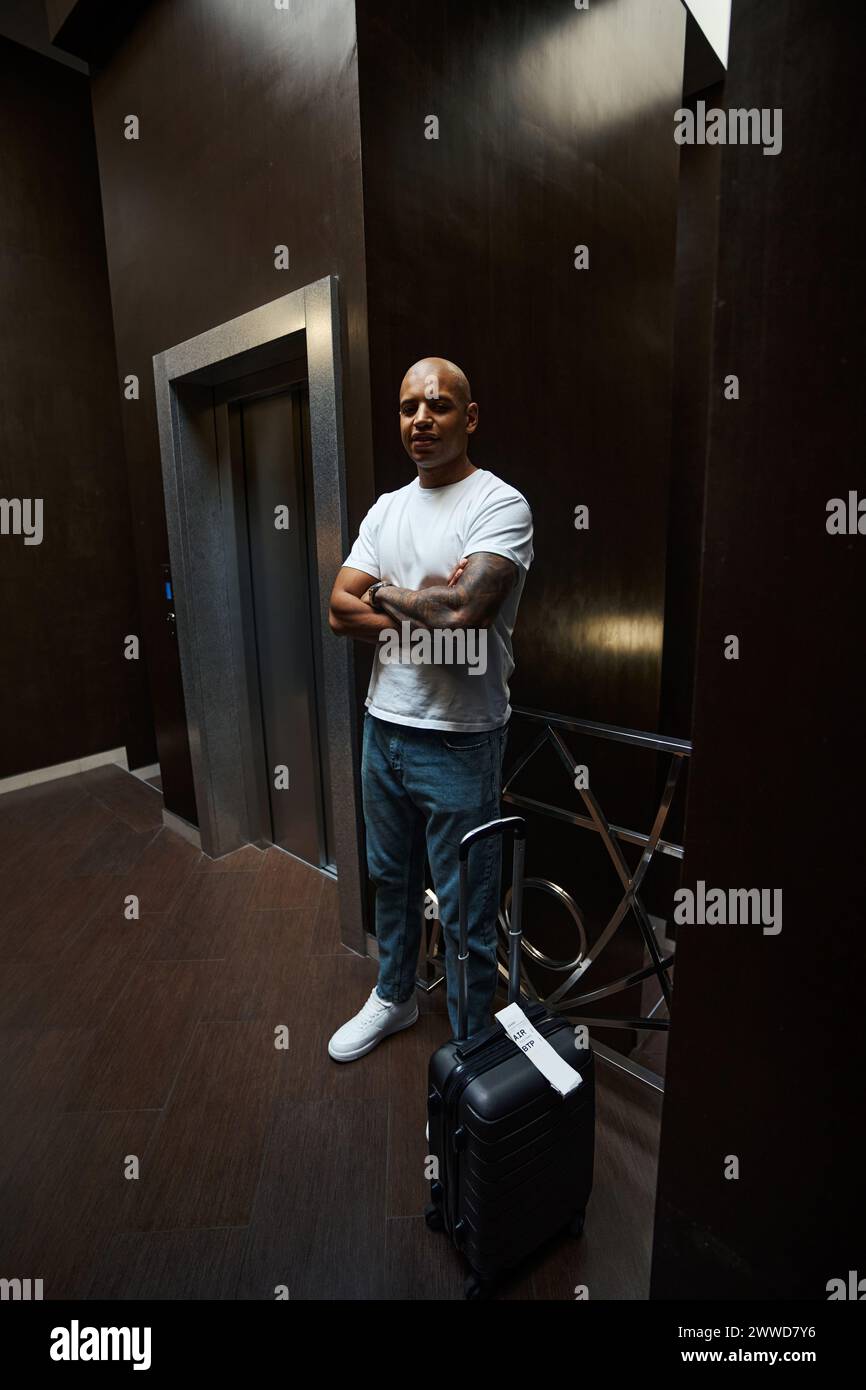Man with suitcase and crossed arms standing near elevator n hall of ...