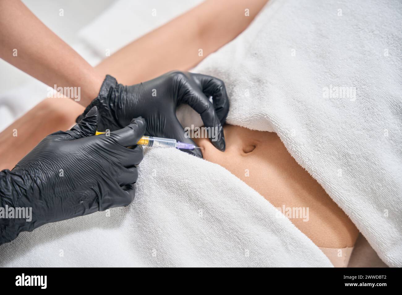 Partial of cosmetologist doing stomach beauty injection with syringe of ...