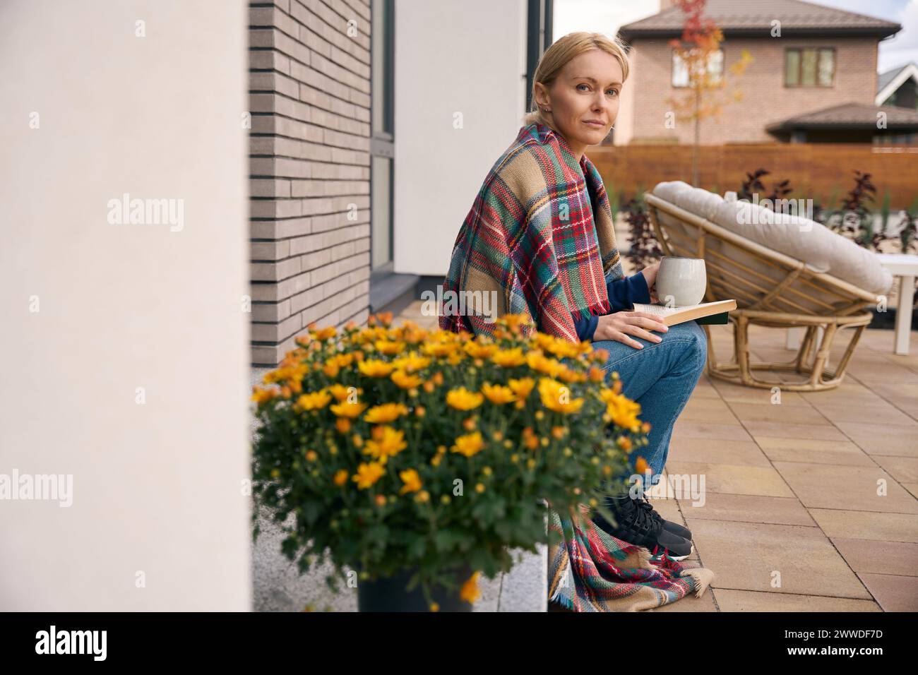 Calm lady sitting outside house while holding cup and book Stock Photo ...