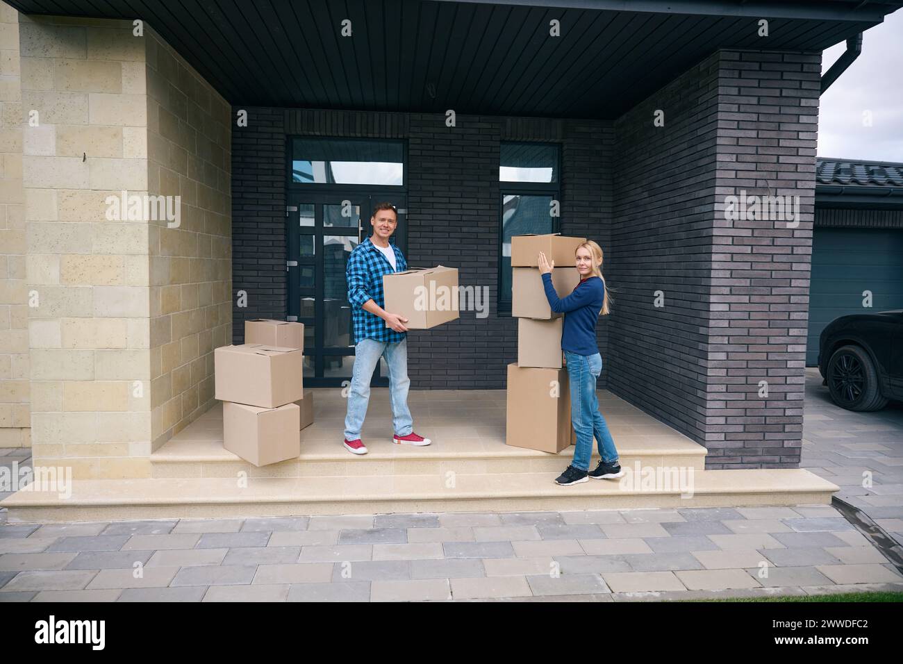 Amused couple arranging boxes on house porch while moving house Stock ...