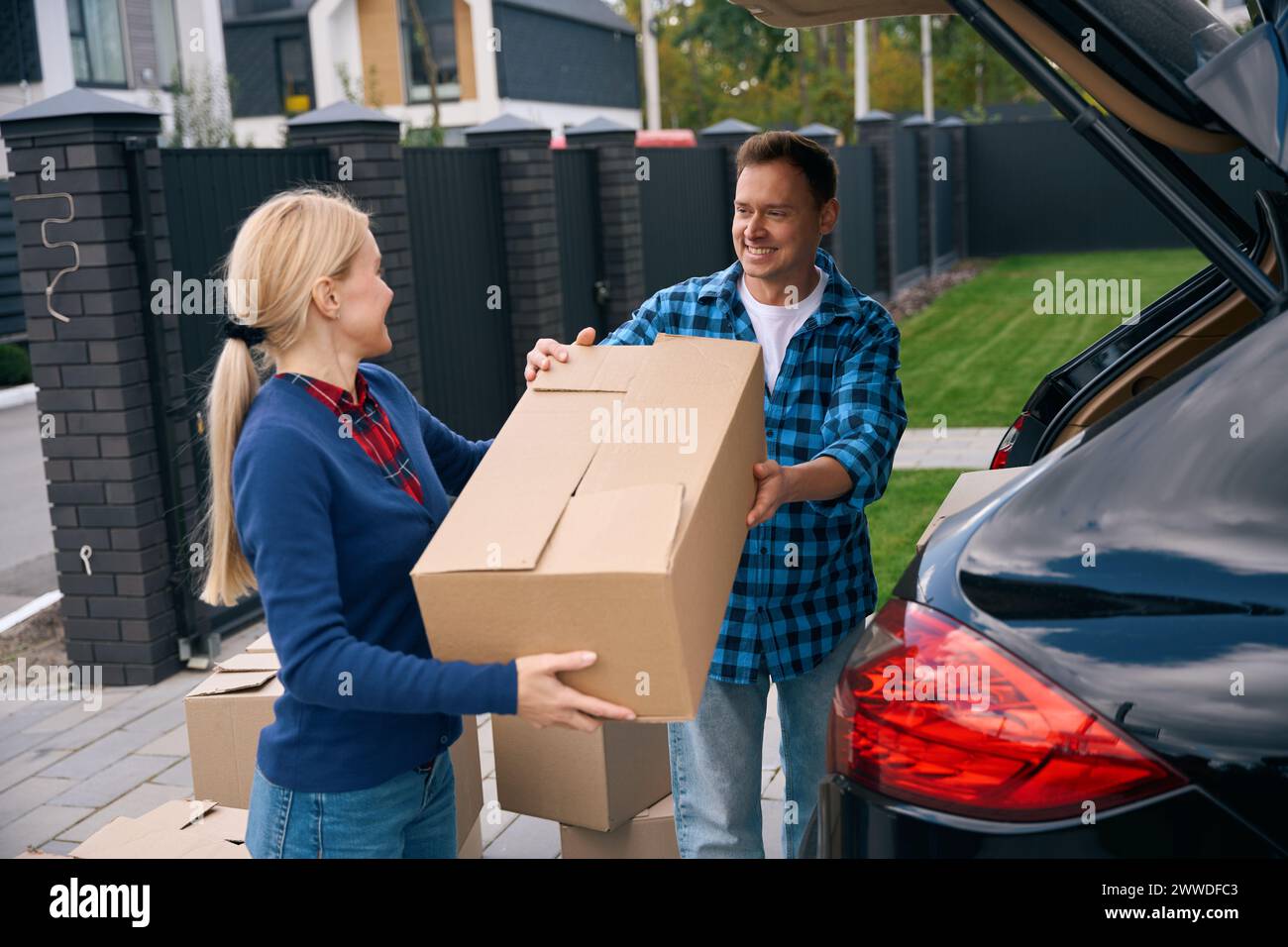 Joyful couple standing and unloading boxes out of car trunk Stock Photo ...