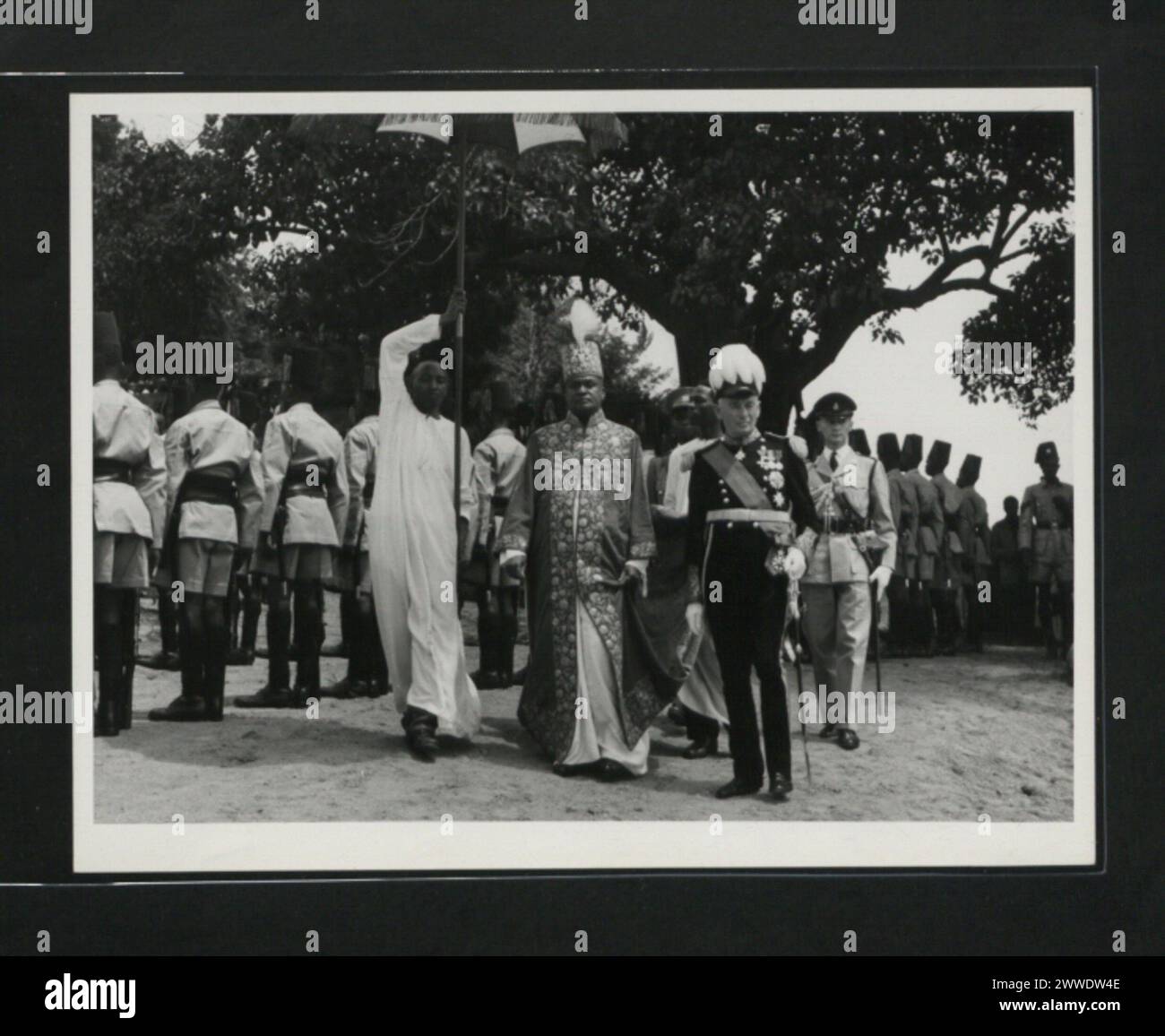 Description: Escorted by an attendant bearing a huge umbrella, the ...
