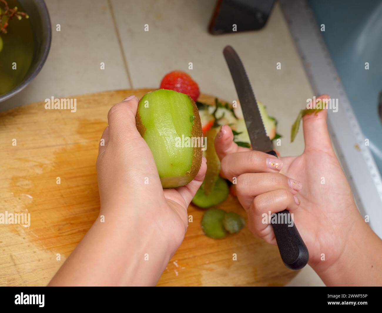 Woman hands peeling a kiwi fruit in the kitchen at home. Woman peeling ...