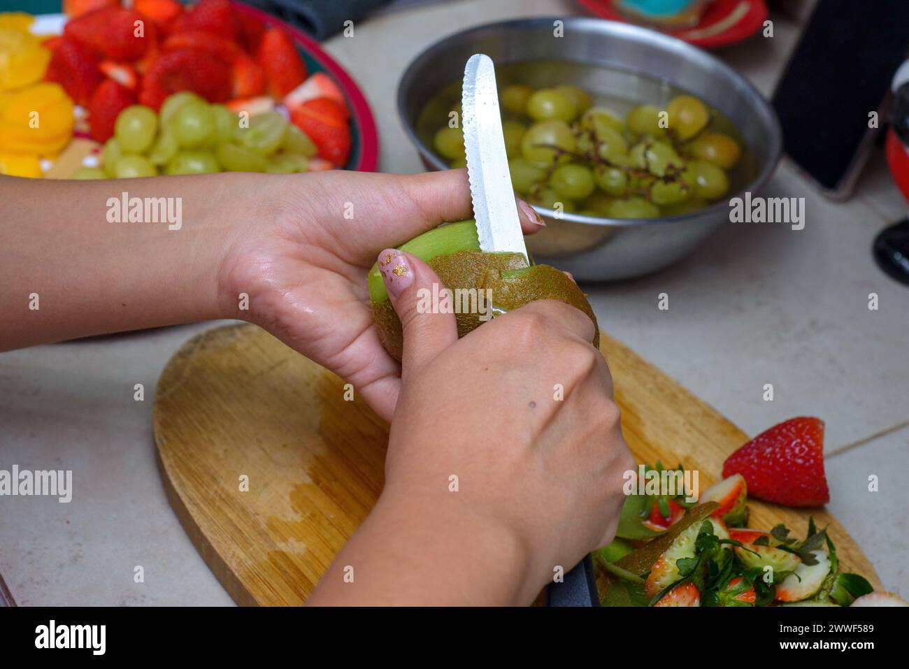 Woman hands peeling a kiwi fruit in the kitchen at home. Woman peeling ...