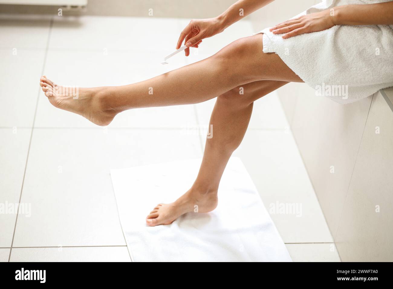 A woman with towel wrapped around waist gestures shaving knee to ankle ...