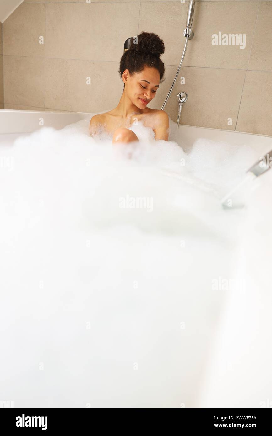 A woman bathing in a tub filled with foam, her head covered in bubbles ...
