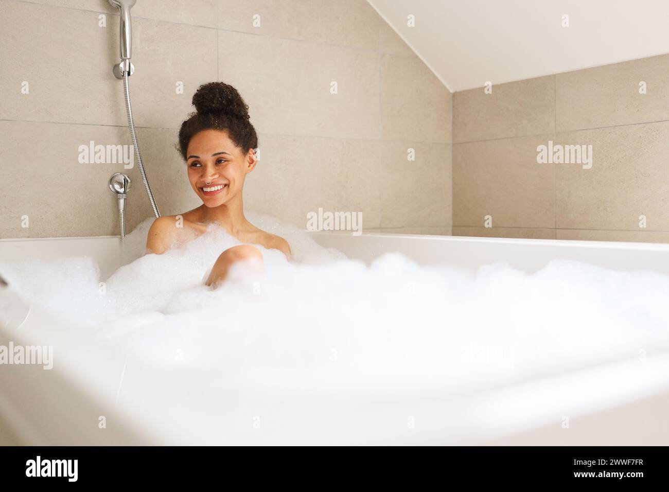 Woman with black hair bathing in foamfilled bathtub, smiling with ...