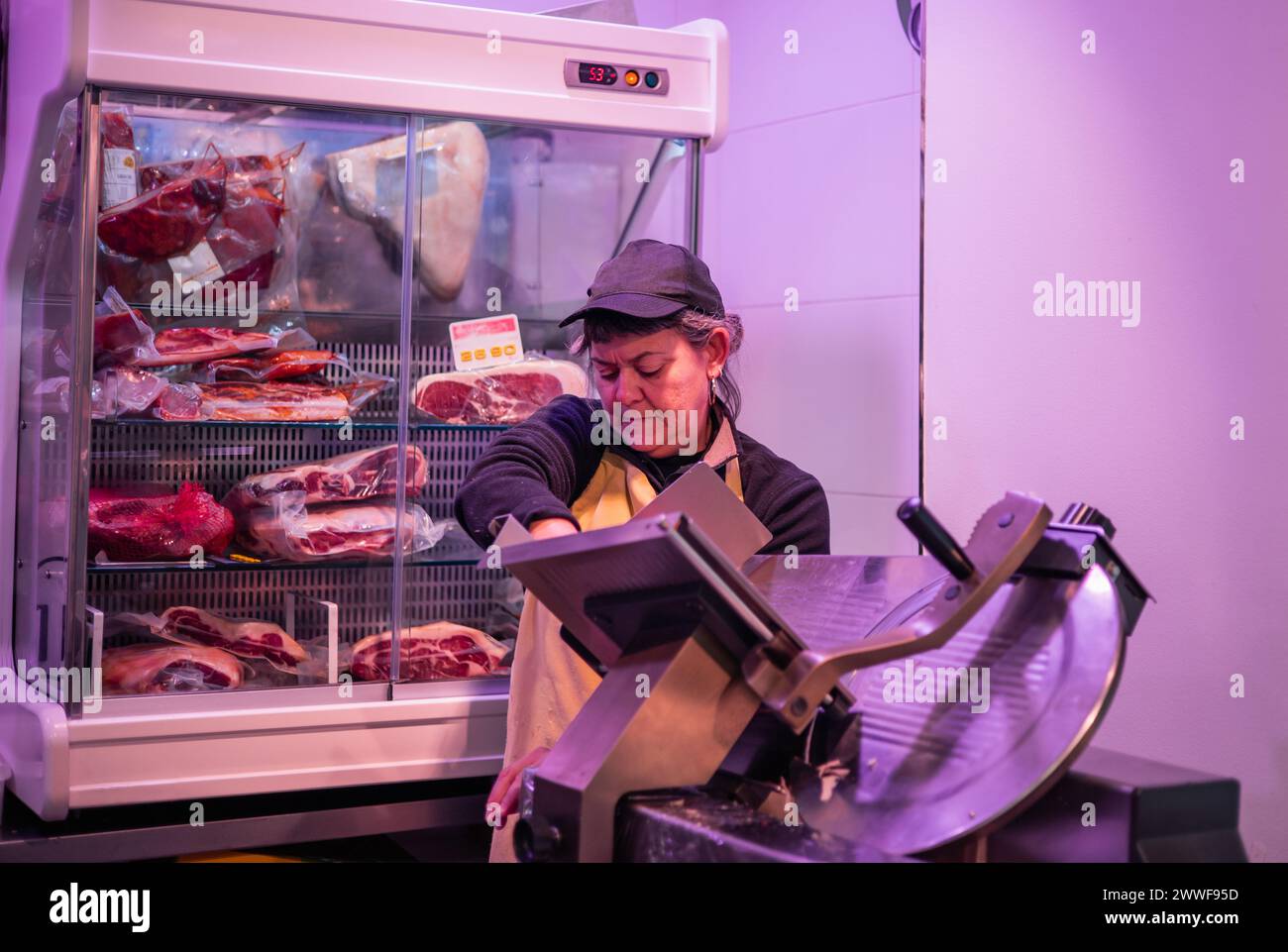 In this image, a female butcher is seen operating an electric meat ...