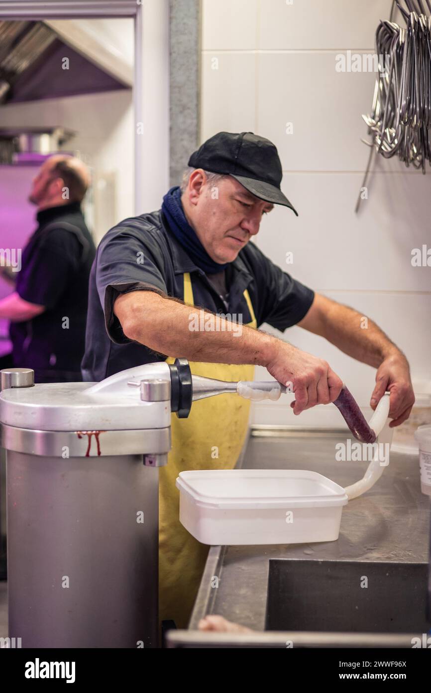 vertical portrait elderly butcher is seen filling sausages with meat ...