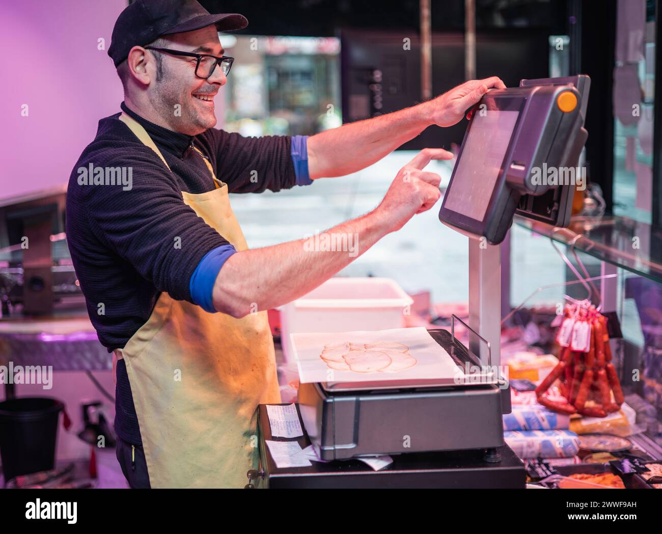 smiling butcher wearing glasses weighing the customer's meat purchase ...
