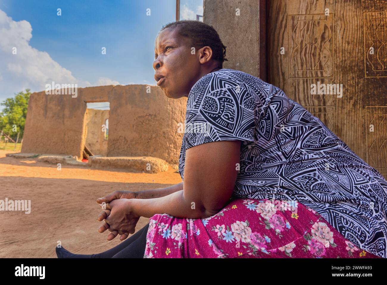 village african woman with braids in front of her home, sited on the ...