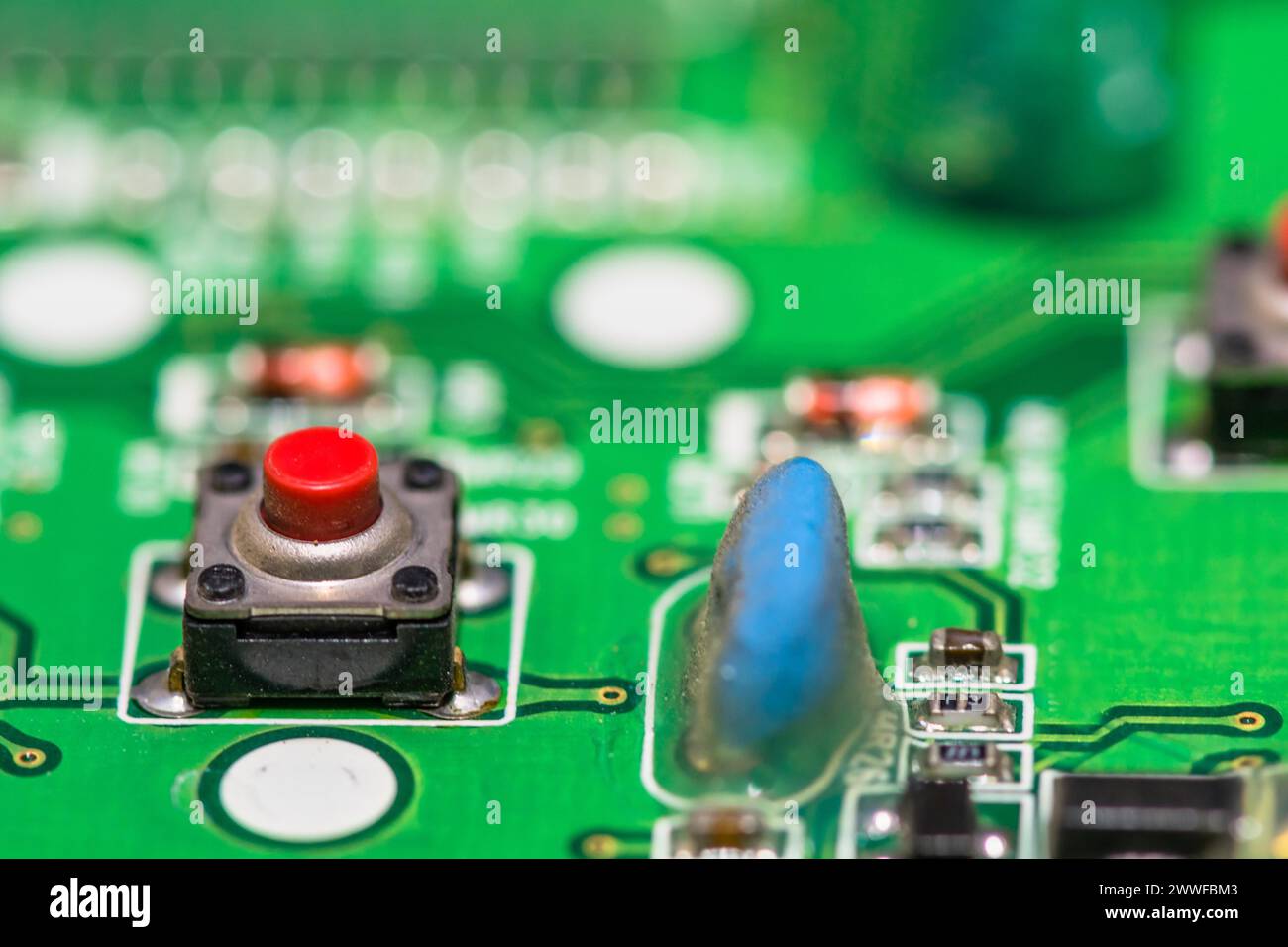 Red reset button mounted on green circuit board next to blue diode ...