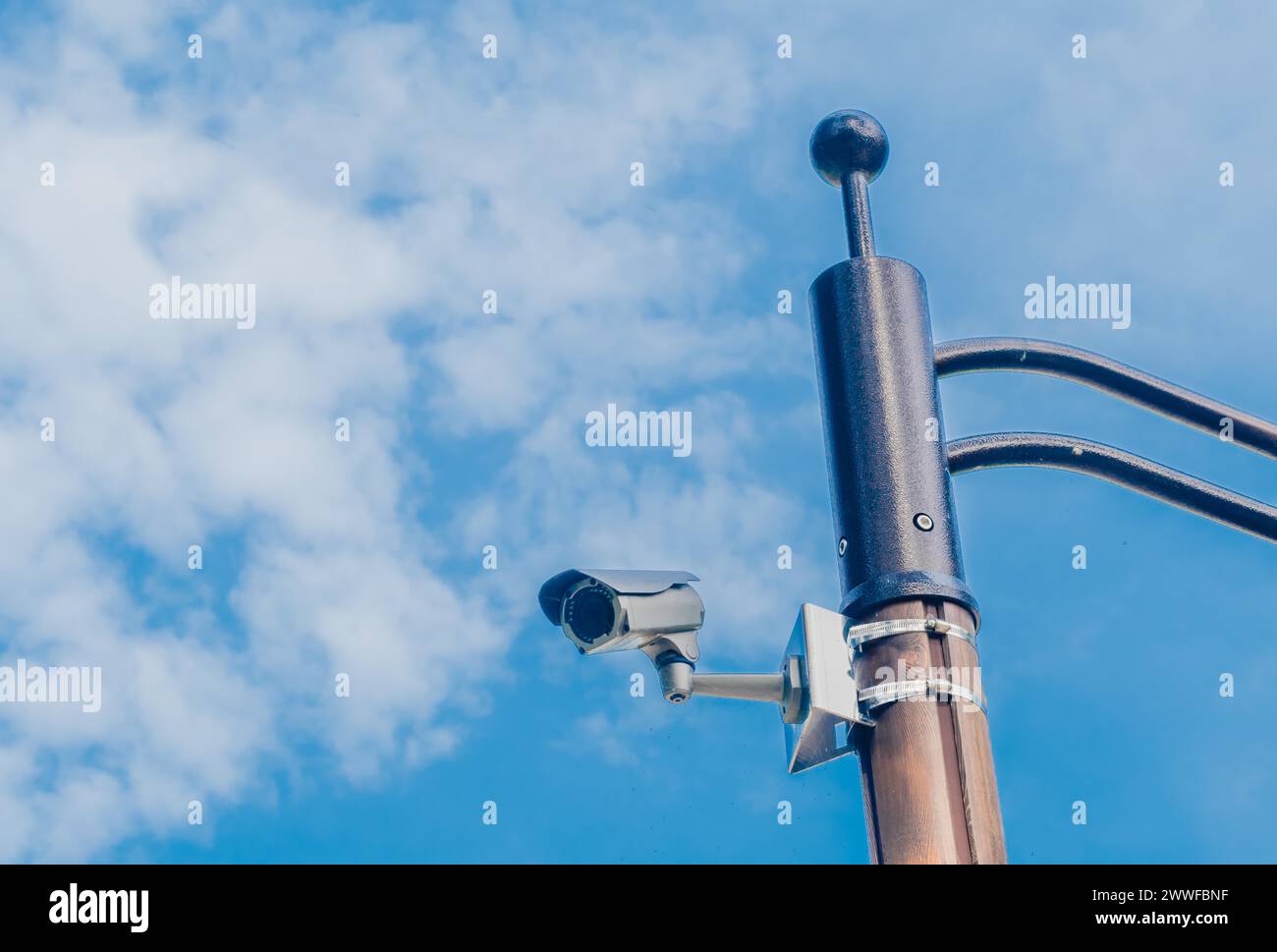 Surveillance camera mounted on metal light pole with blue sky and puffy ...