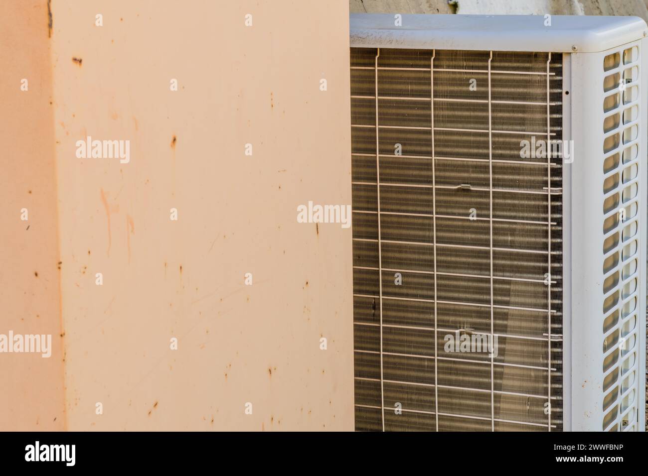 Closeup of air conditioner condenser unit behind a pinkish colored wall ...