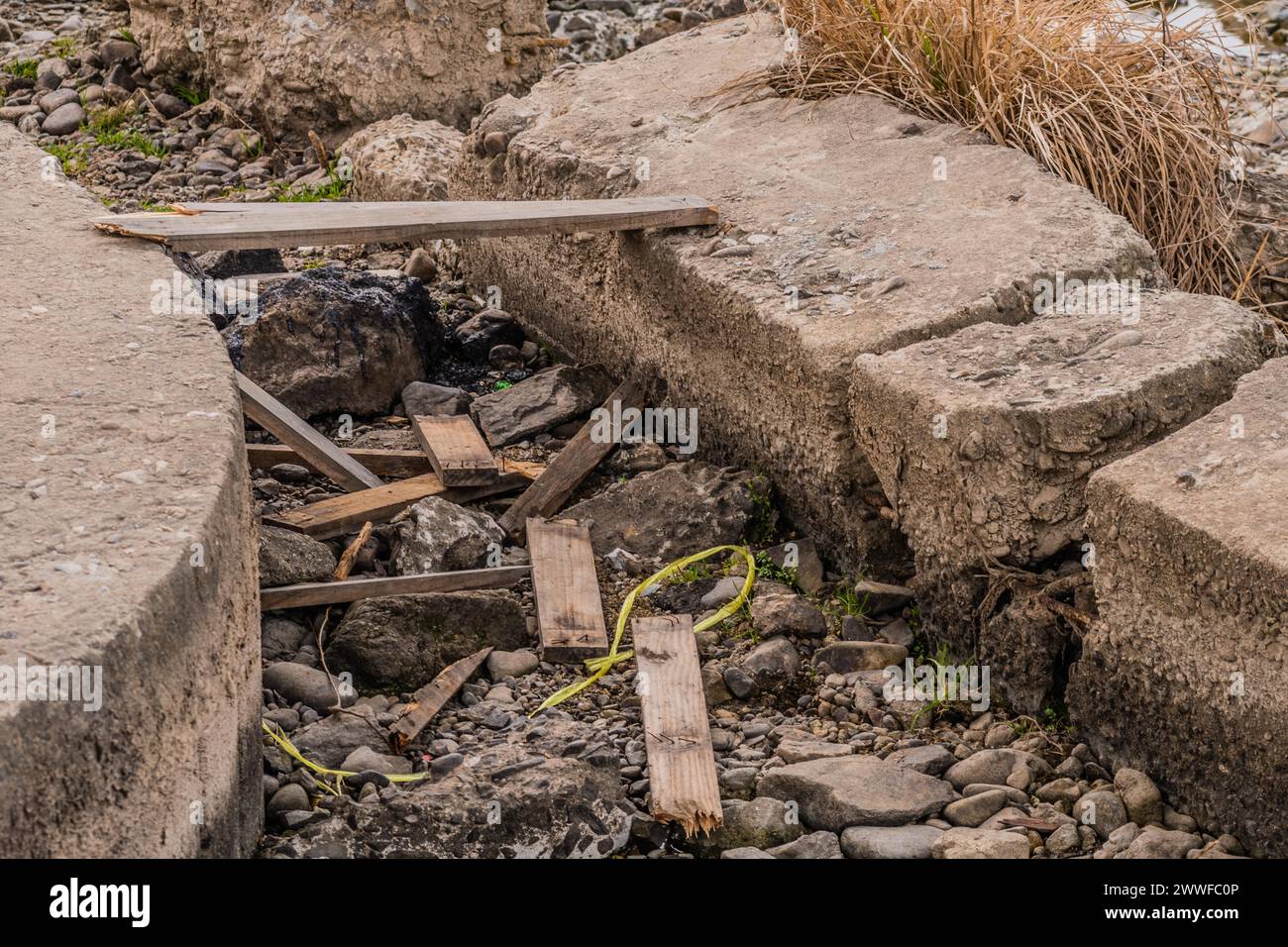 Damaged small concrete bridge with wooden planks over a stream bed, in ...
