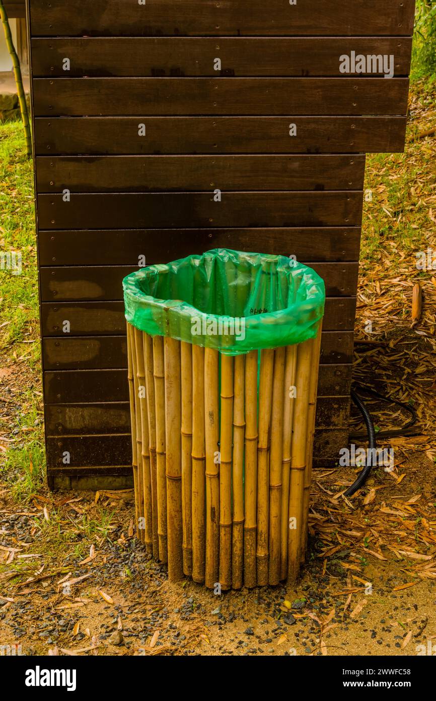 A green-topped trash can with a bamboo exterior stands beside a wooden ...