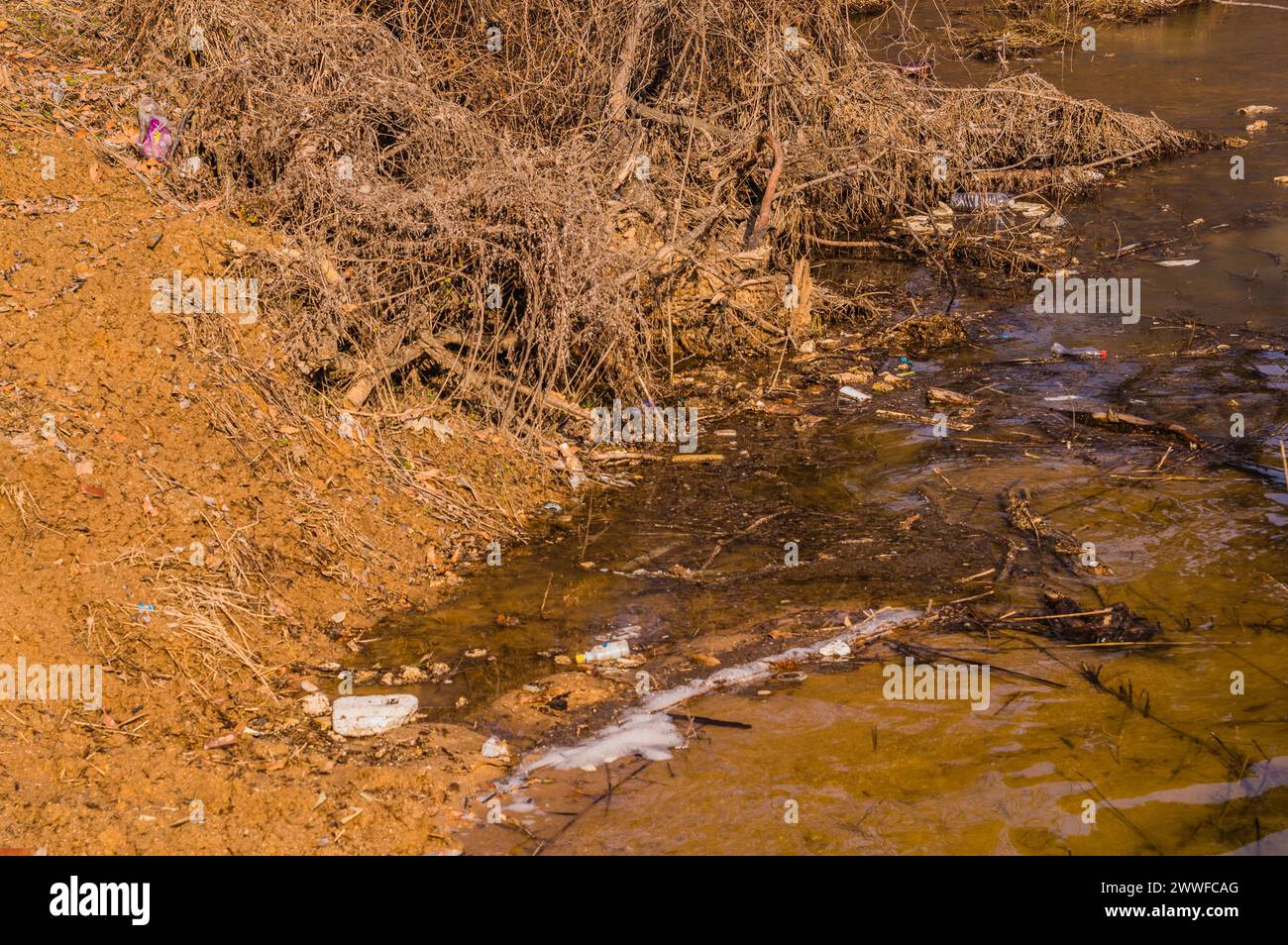 A small stream flows through a muddy landscape with signs of vegetation erosion, in South Korea ...