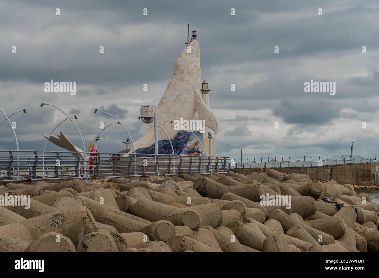 Mosaic fish sculpture on the harbor edge with street lamps and cloudy ...
