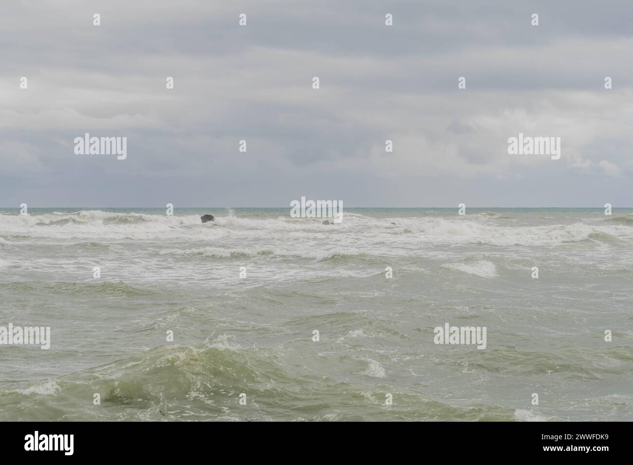 Choppy ocean waves under a cloudy sky with a solitary rock visible, in ...