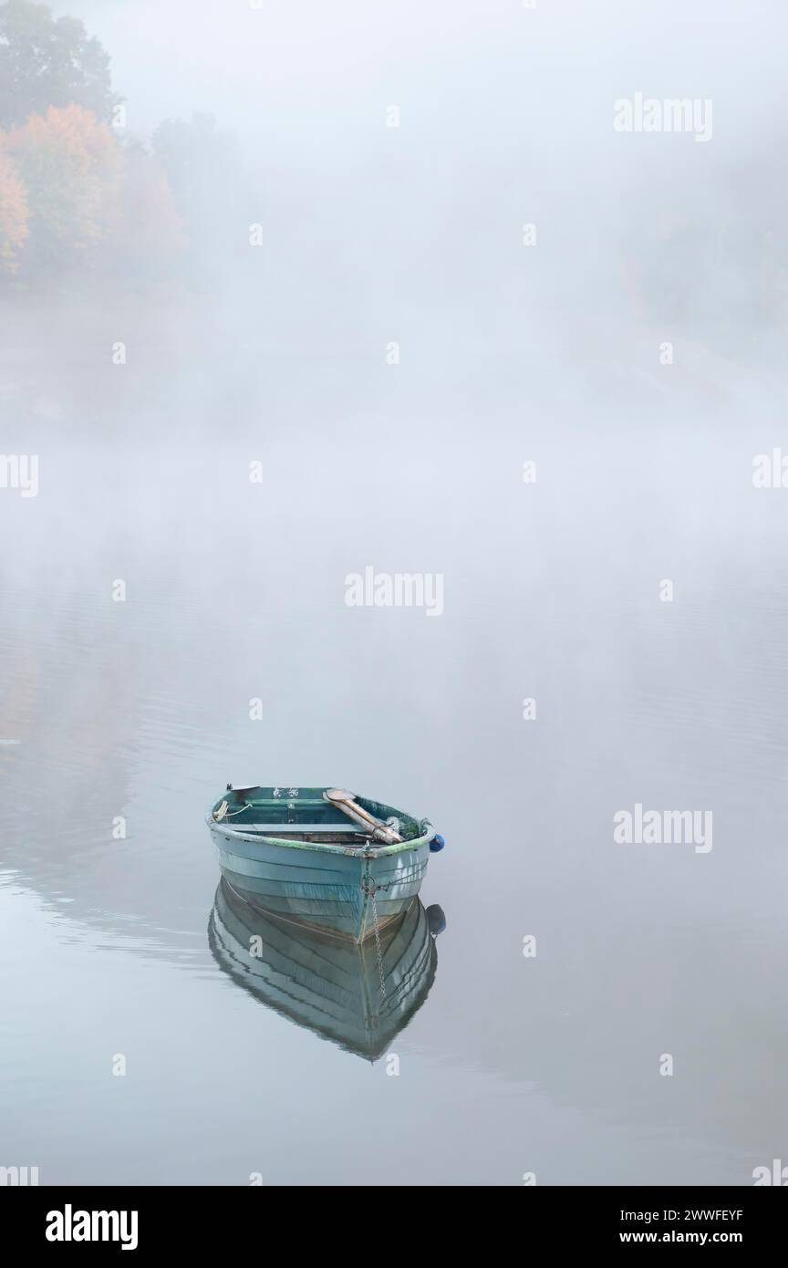 Wooden boat floating in the water, surrounded by fog, in the background ...
