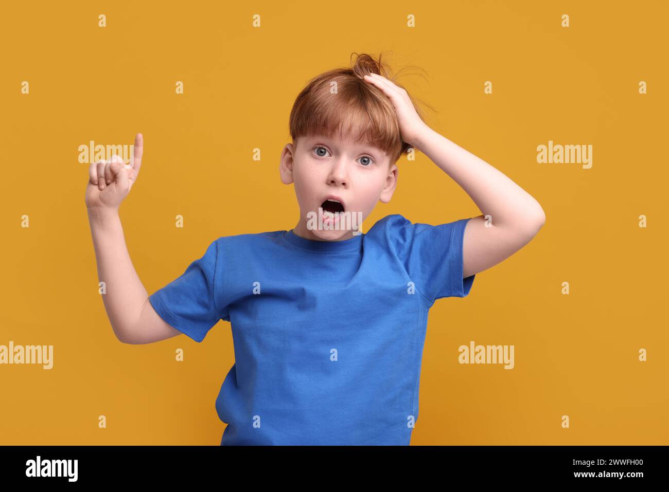 Surprised little boy pointing at something on orange background Stock ...