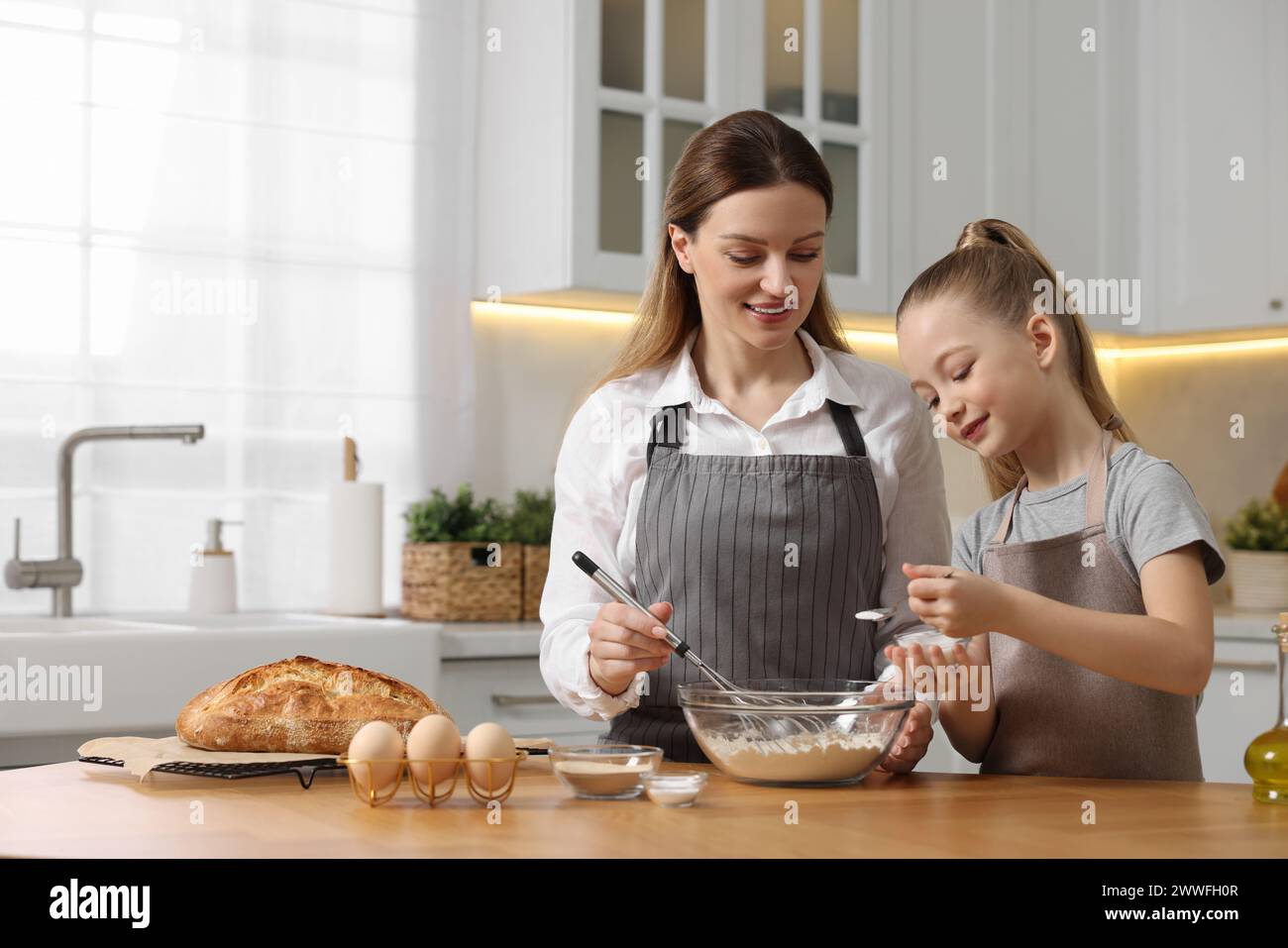 Making bread. Mother and her daughter preparing dough at wooden table ...