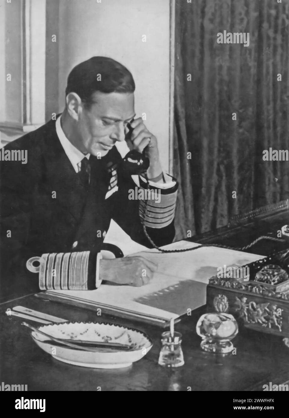 A photograph, taken around 1940, shows King George VI in his study, on ...