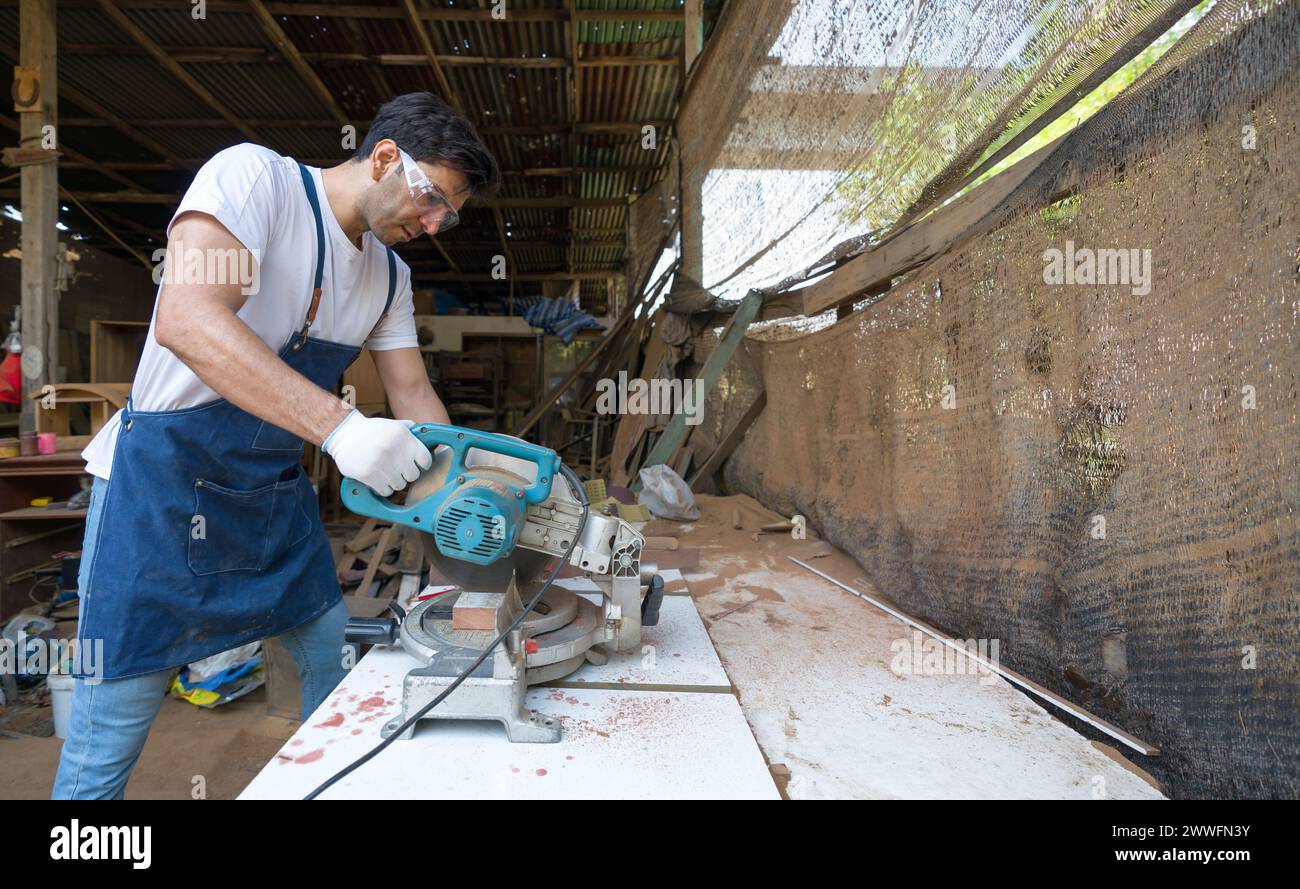 Young carpentry using a power miter saw to cut a piece of wood ...