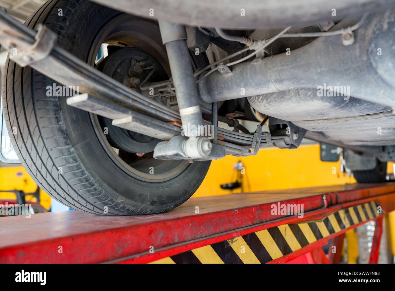 A car is on a lift showing its underside with a wheel, leaf spring and ...