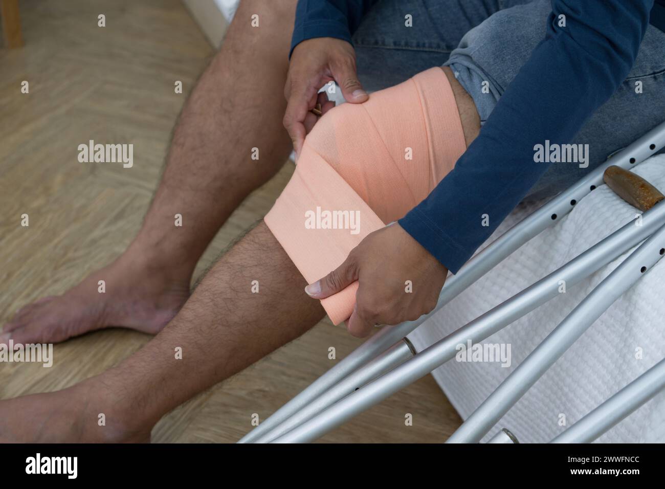 A man with a broken knee sitting on his bed. He leans on crutches ...