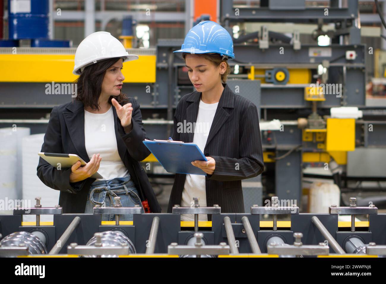 Two women operate machinery in a factory, wearing safety gear and ...
