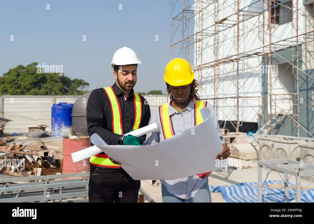Two construction worker looking at a floor plan, standing in front of a ...
