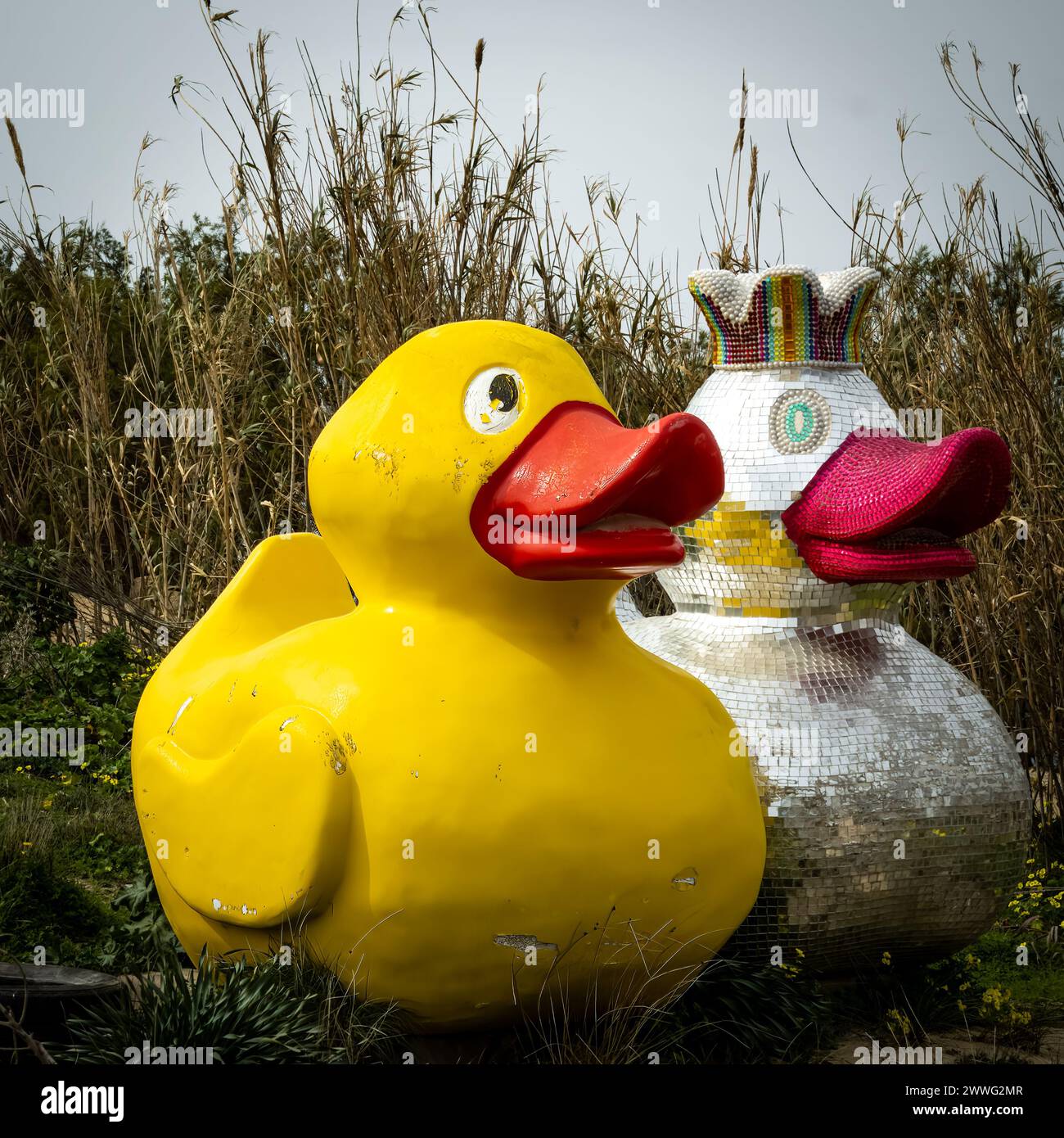 A large yellow duck sculpture next to a mosaic rooster in an outdoor ...