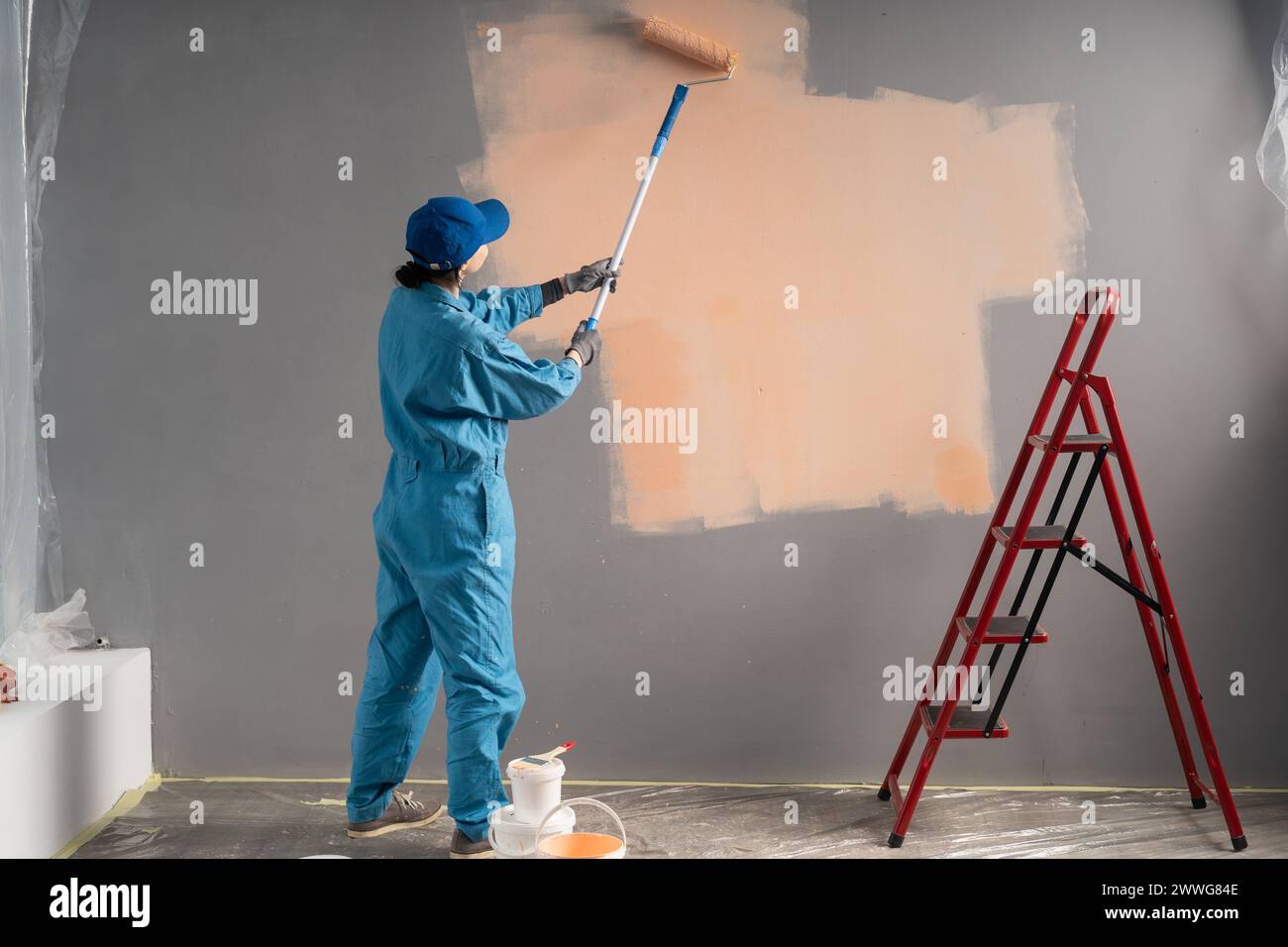 Builder or painter in cap Paints walls with long painting roller ...
