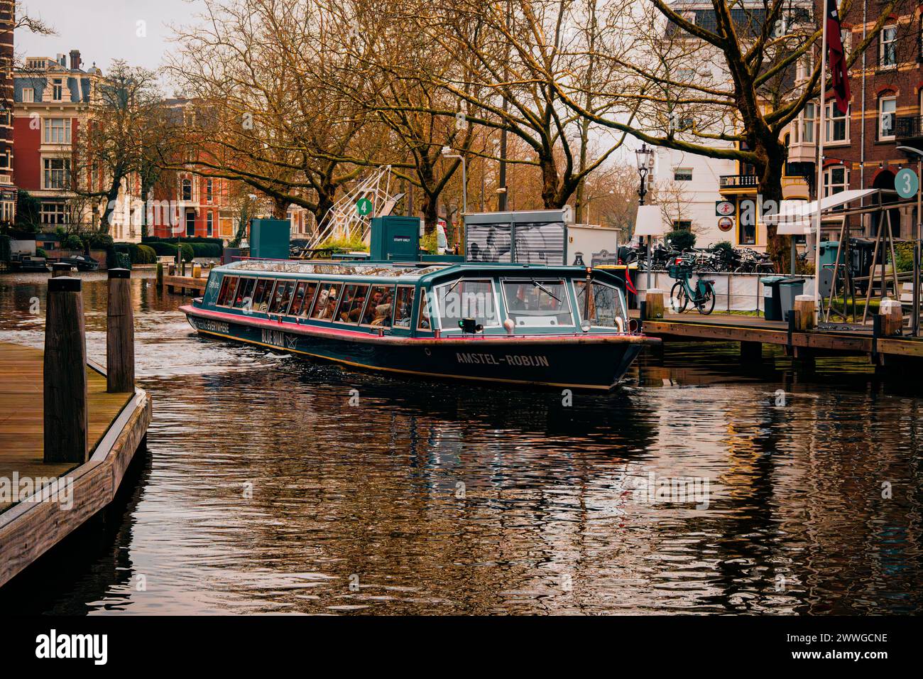 A glass-roofed tour boat cruises along the calm waters of an urban ...