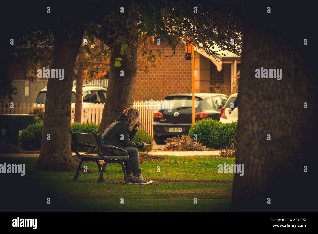 A lone individual deep in thought on a park bench, surrounded by nature ...